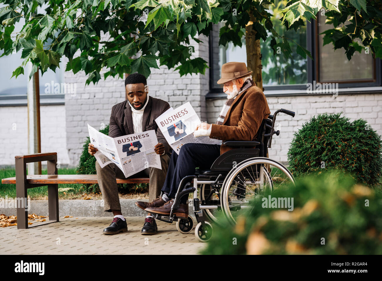 Senior Disabled Man In Wheelchair And African American Man Reading