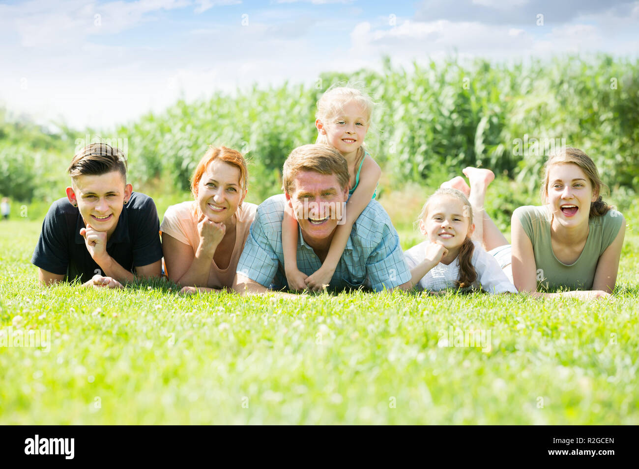 Portrait of friendly large family of six lying together on green lawn ...
