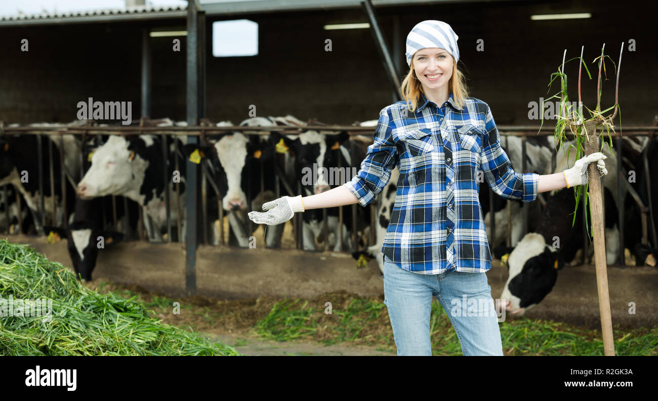 Young female worker collecting grass with pitchfork in barn Stock Photo ...