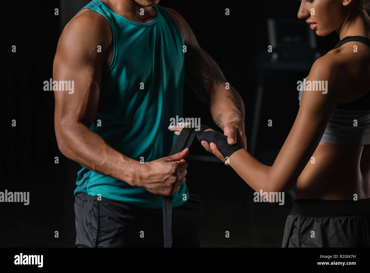 cropped image of male trainer with tattooed hand wrapping female boxer ...
