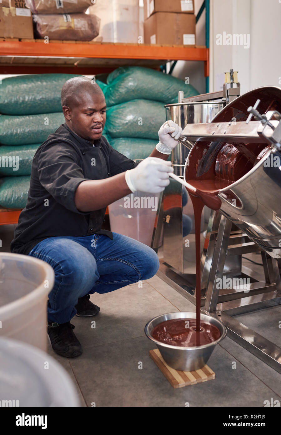Confectionary factory worker pouring melting chocolate into a bowl ...
