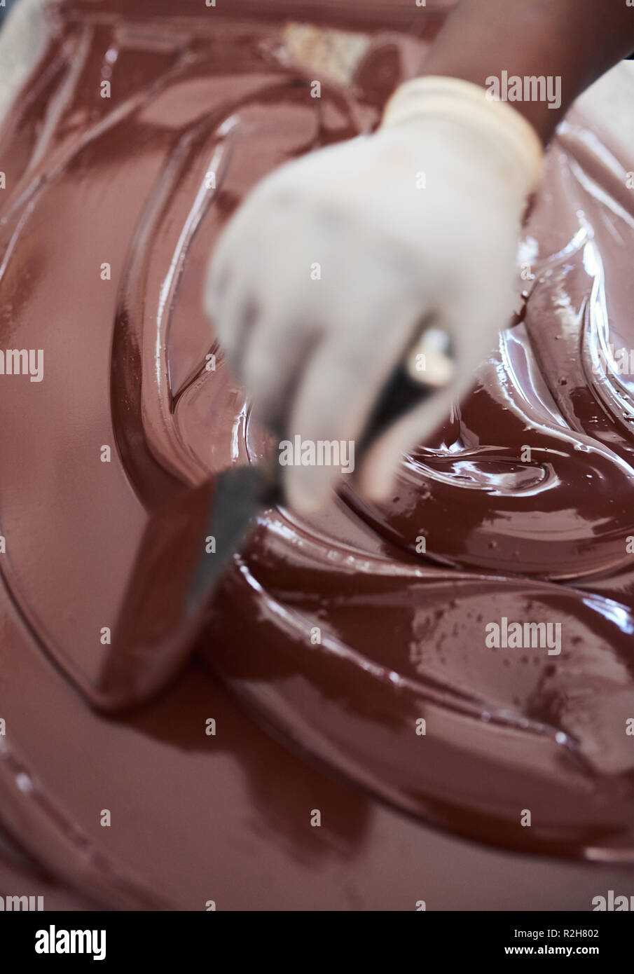 Confectionary factory worker mixing melted chocolate with a spatula ...