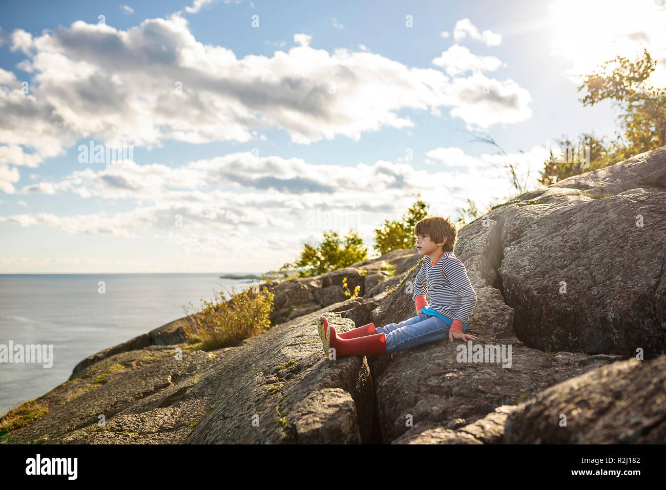 Boy sitting on rocks by a lake, Lake Superior Provincial Park, United ...