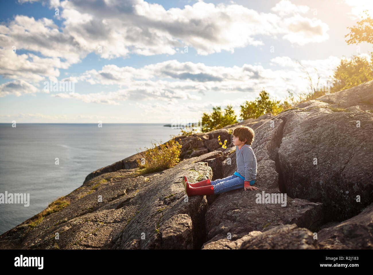 Boy sitting on rocks by a lake, Lake Superior Provincial Park, United ...