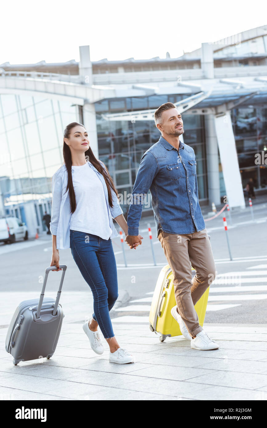 A couple of tourists crossing pedestrian, holding hands and pulling ...