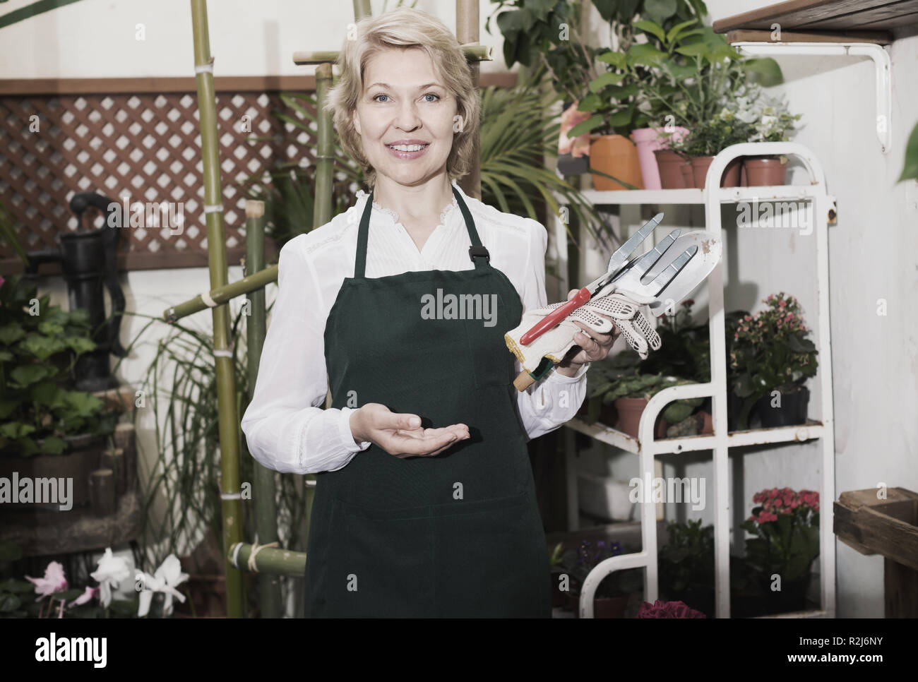 Cheerful female florist wearing an apron and happily standing amongst ...