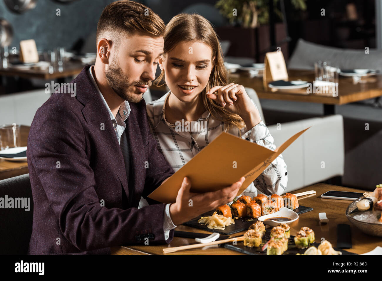Beautiful young adult couple looking in menu to order dinner in ...