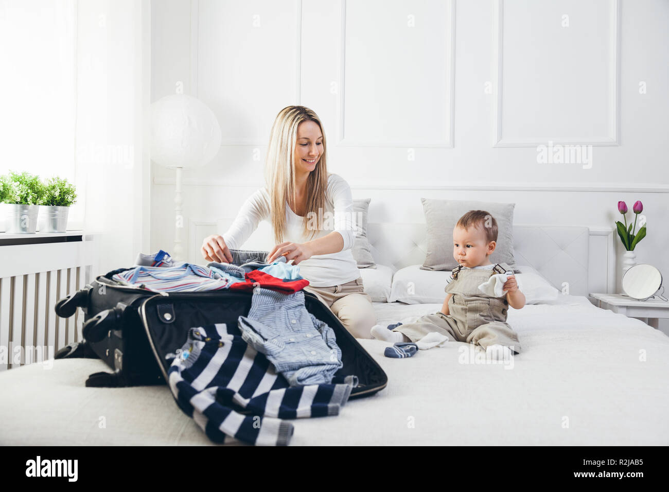 Travelling with kids. Happy mother with her child packing clothes for ...