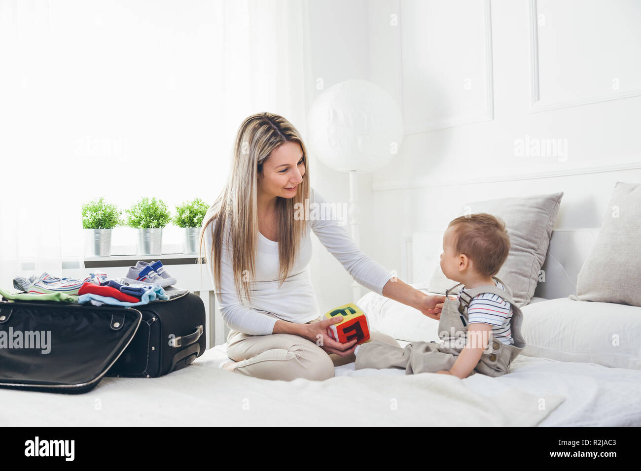 Travelling with kids. Happy mother with her child packing clothes for ...