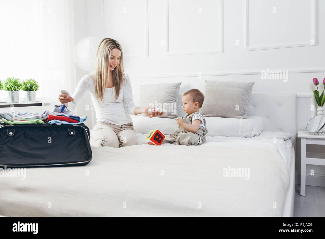 Travelling with kids. Happy mother with her child packing clothes for ...