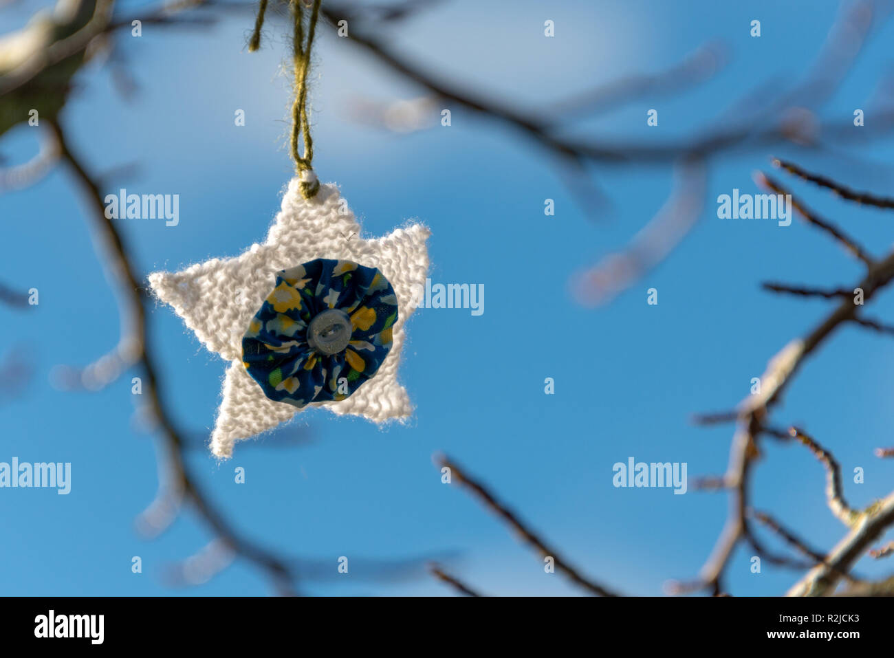 knitted woollen white CHristmas star with green twine hanging from bare ...