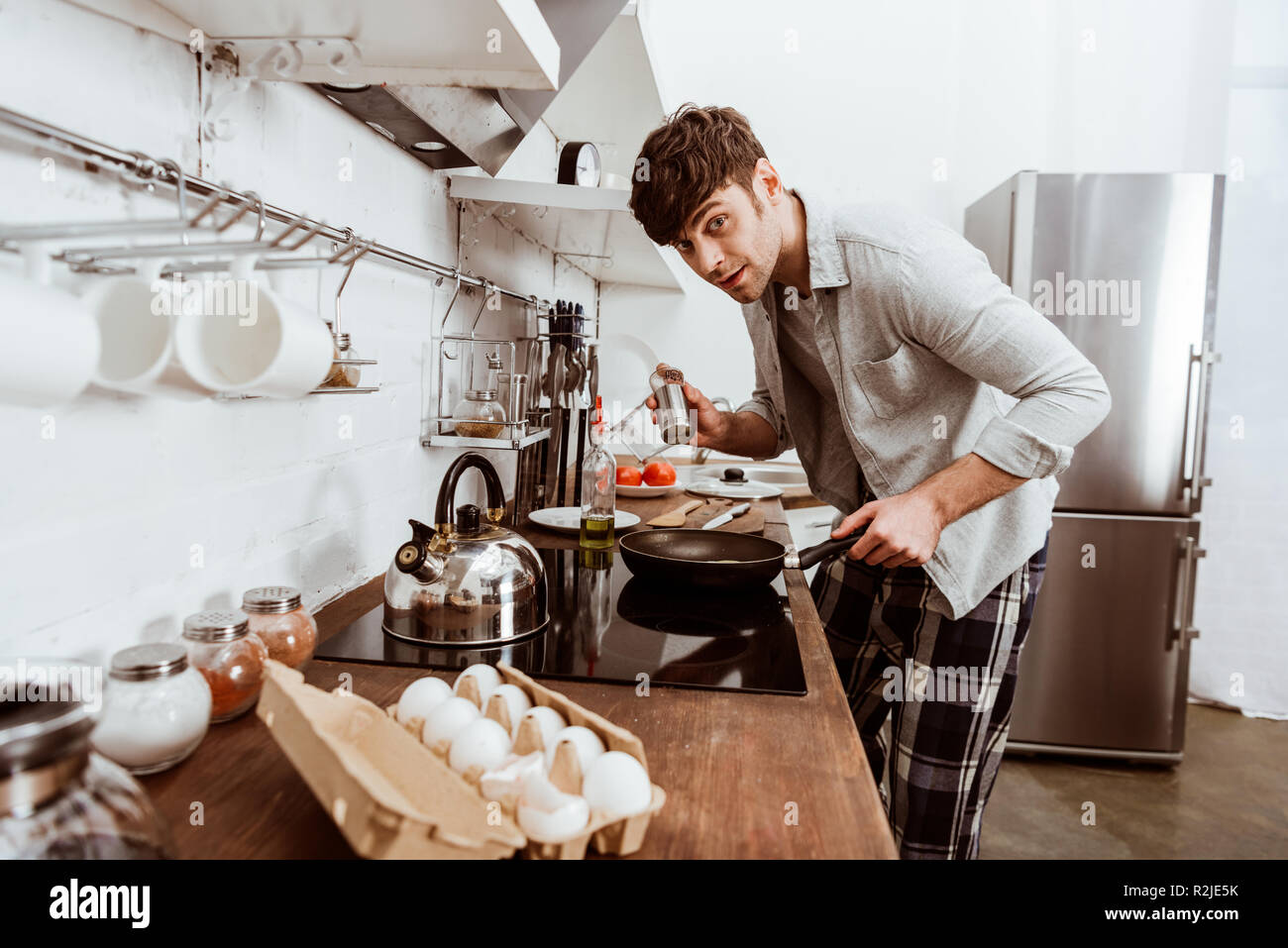 selective focus of young man cooking scrambled eggs on frying pan in ...