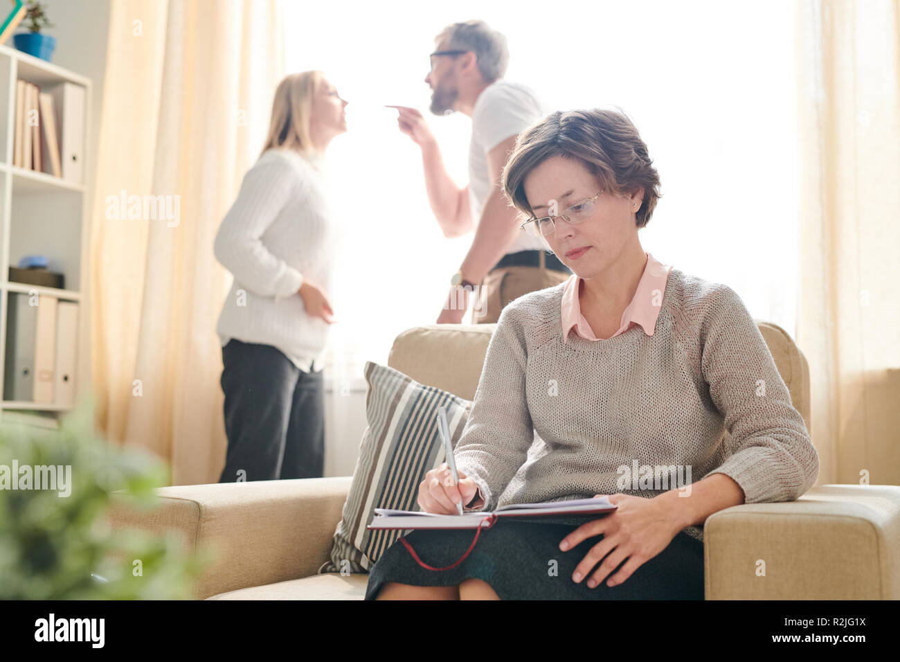 Psychologist making notes while couple fighting Stock Photo - Alamy