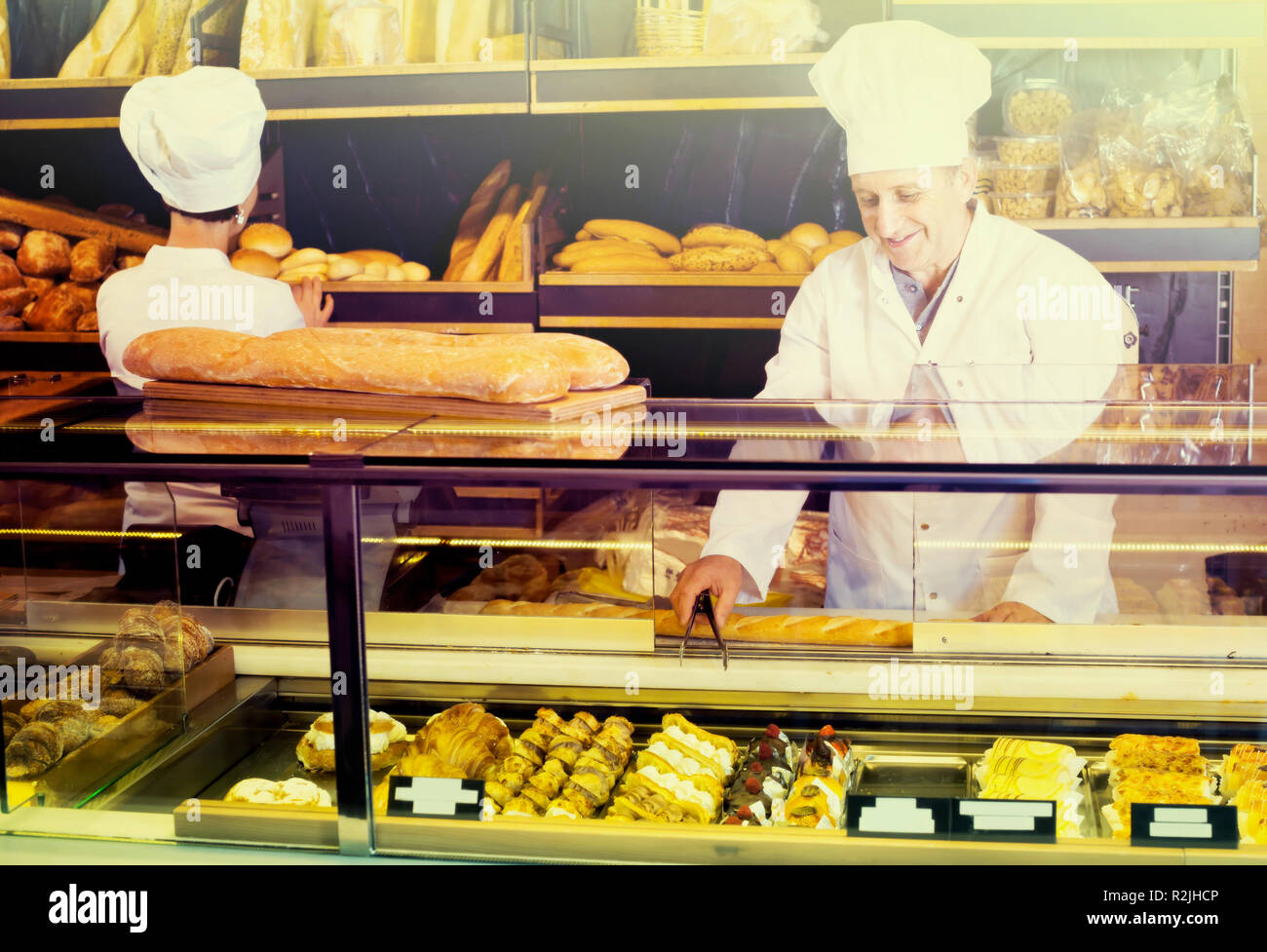 Two positive bakers at the counter with tasty bread products at bakery ...