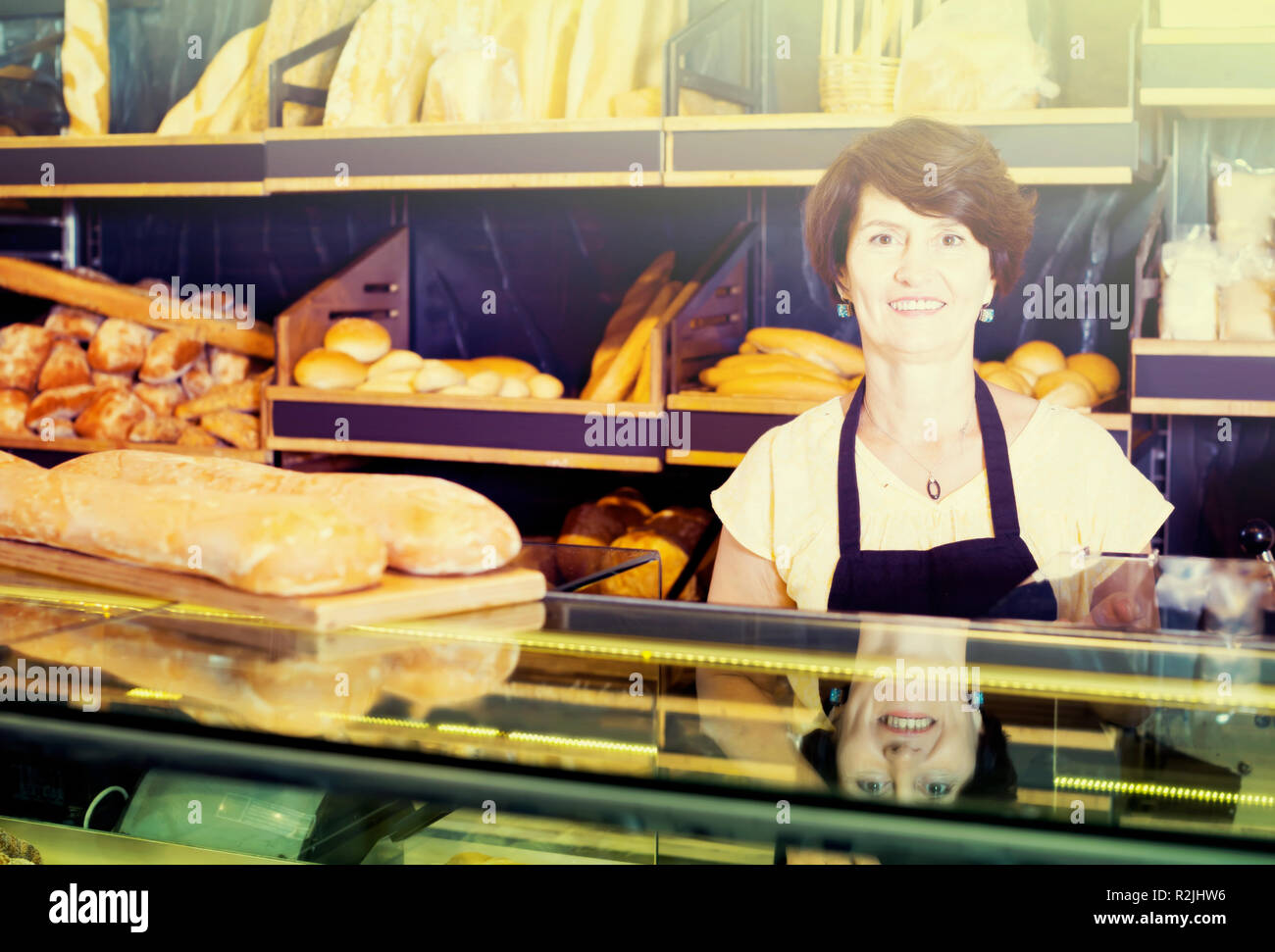 Portrait of positive female baker with fresh bread smiling in bakery ...