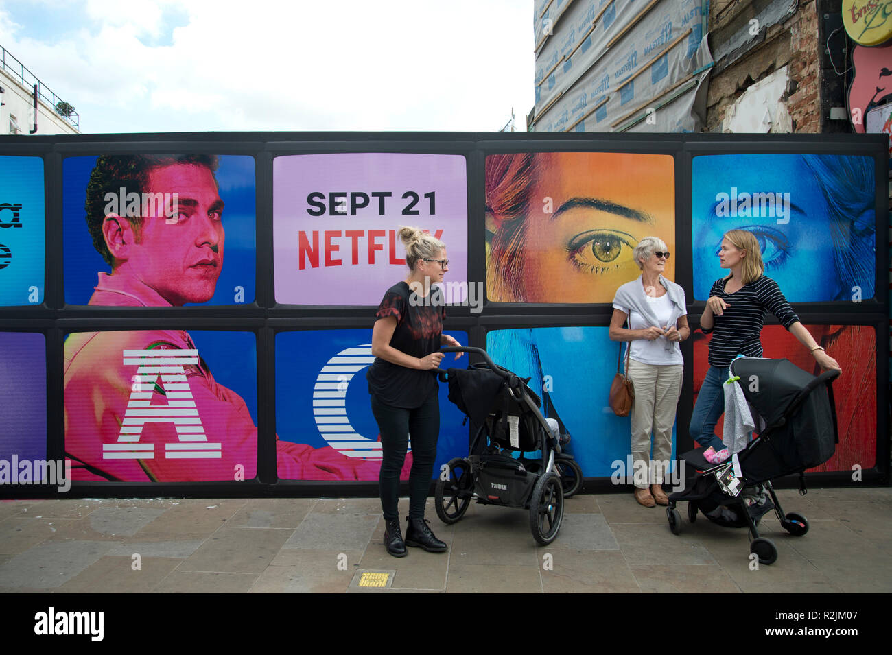 Hackney. Broadway market. Women with pushchairs in front of an advert ...