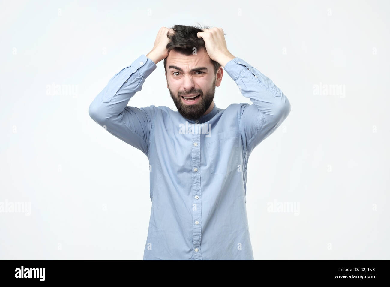Young man with dark hair and beard wears blue shirt looks angry, lips ...