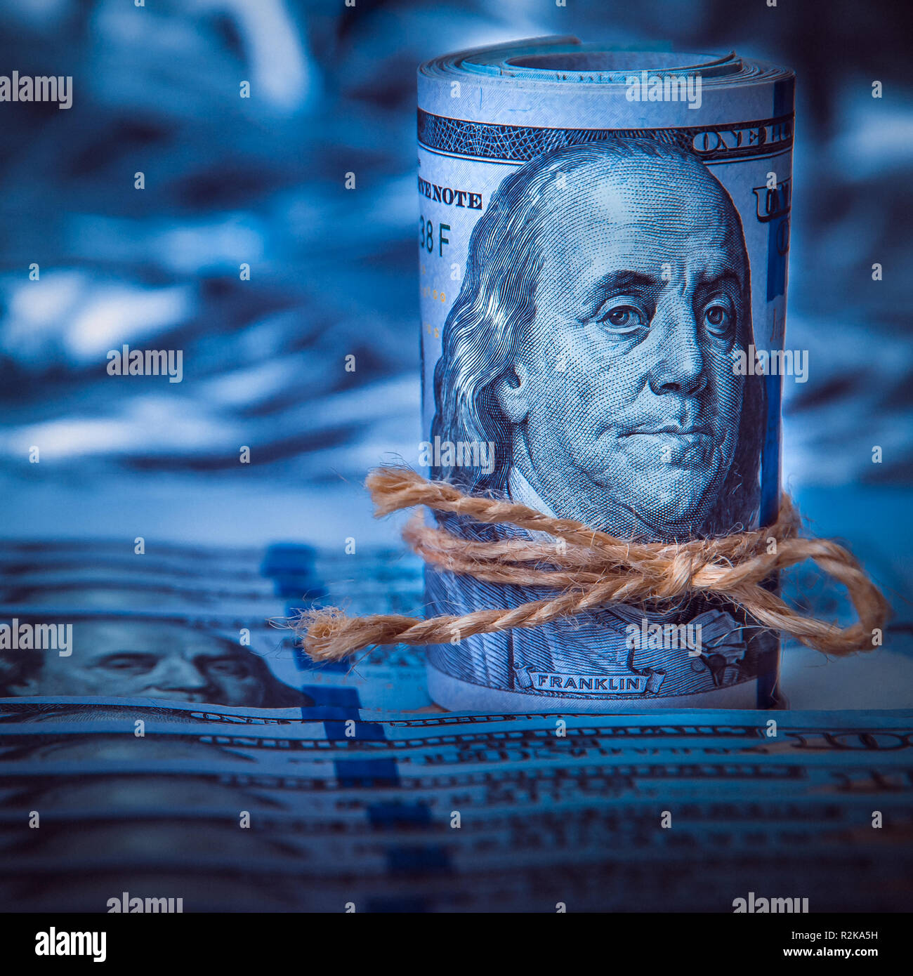 A roll of dollars on the background of scattered hundred dollar bills ...