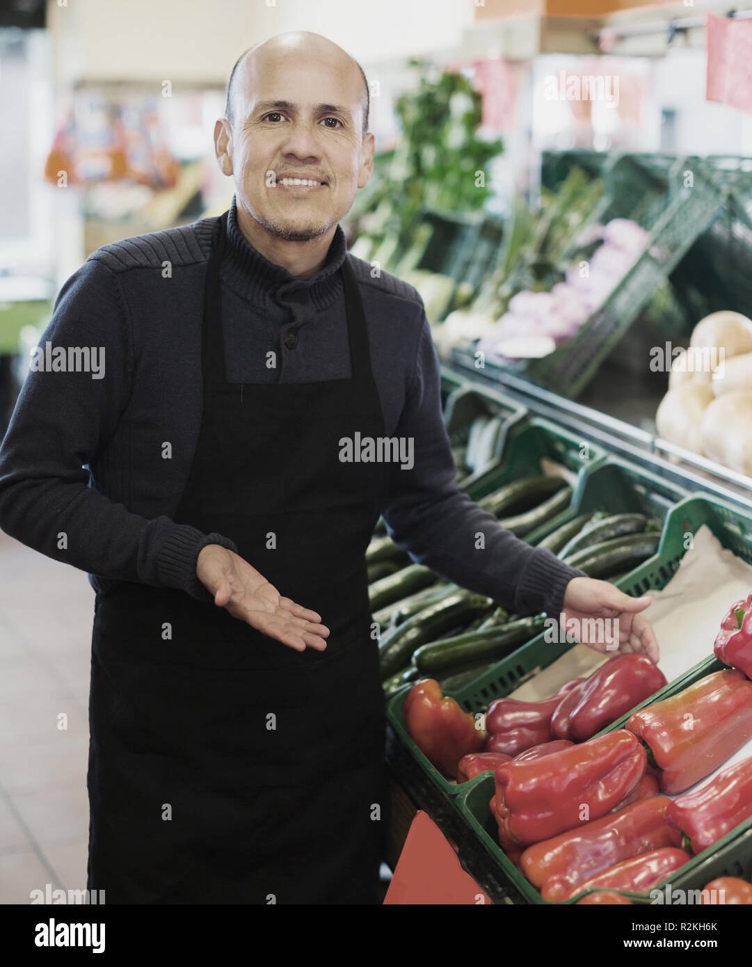 Charming senior salesman posing near display with different vegetables ...