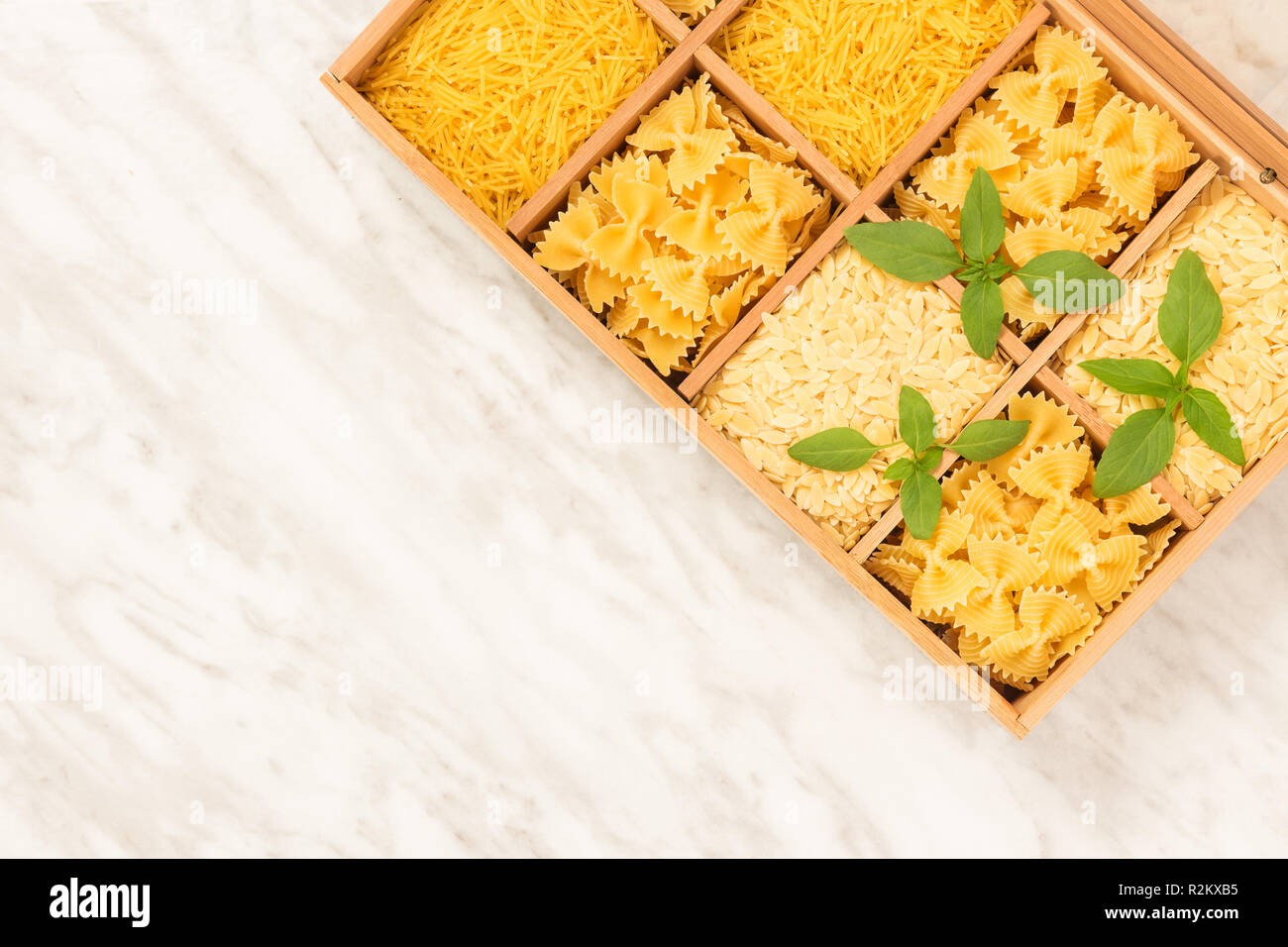Wooden storage box with different types of pasta, on marble background ...
