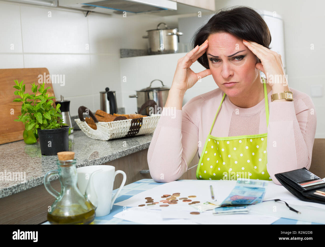 Miserable housewife sitting with bills and money in kitchen Stock Photo ...