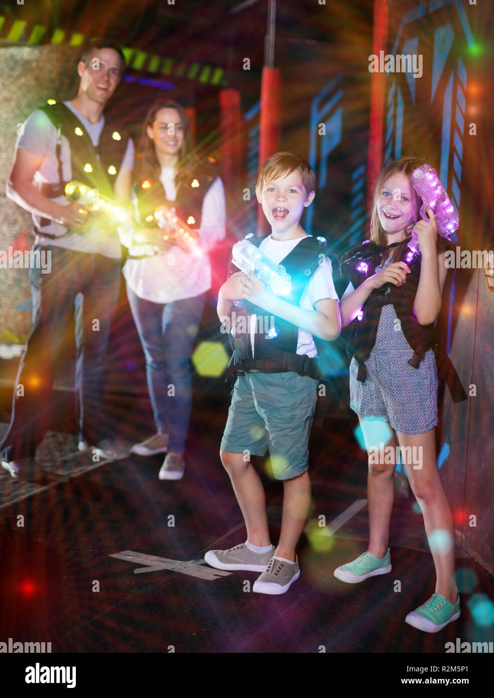 Cheerful little boy and girl having fun with adults on dark lasertag ...