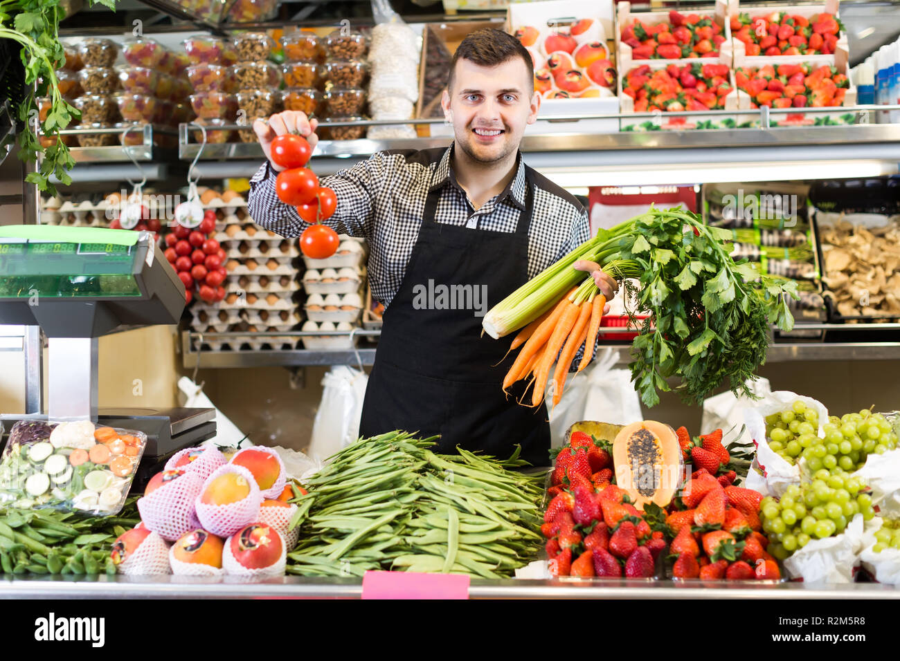 friendly man seller showing assortment of fruits and vegetables in the ...