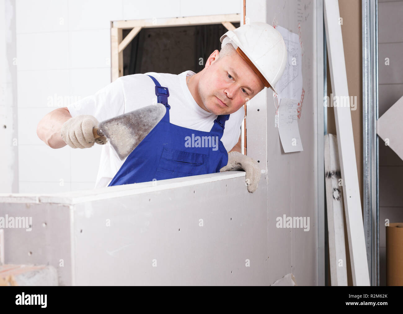 Confident builder filling gaps on drywall element with setting compound ...