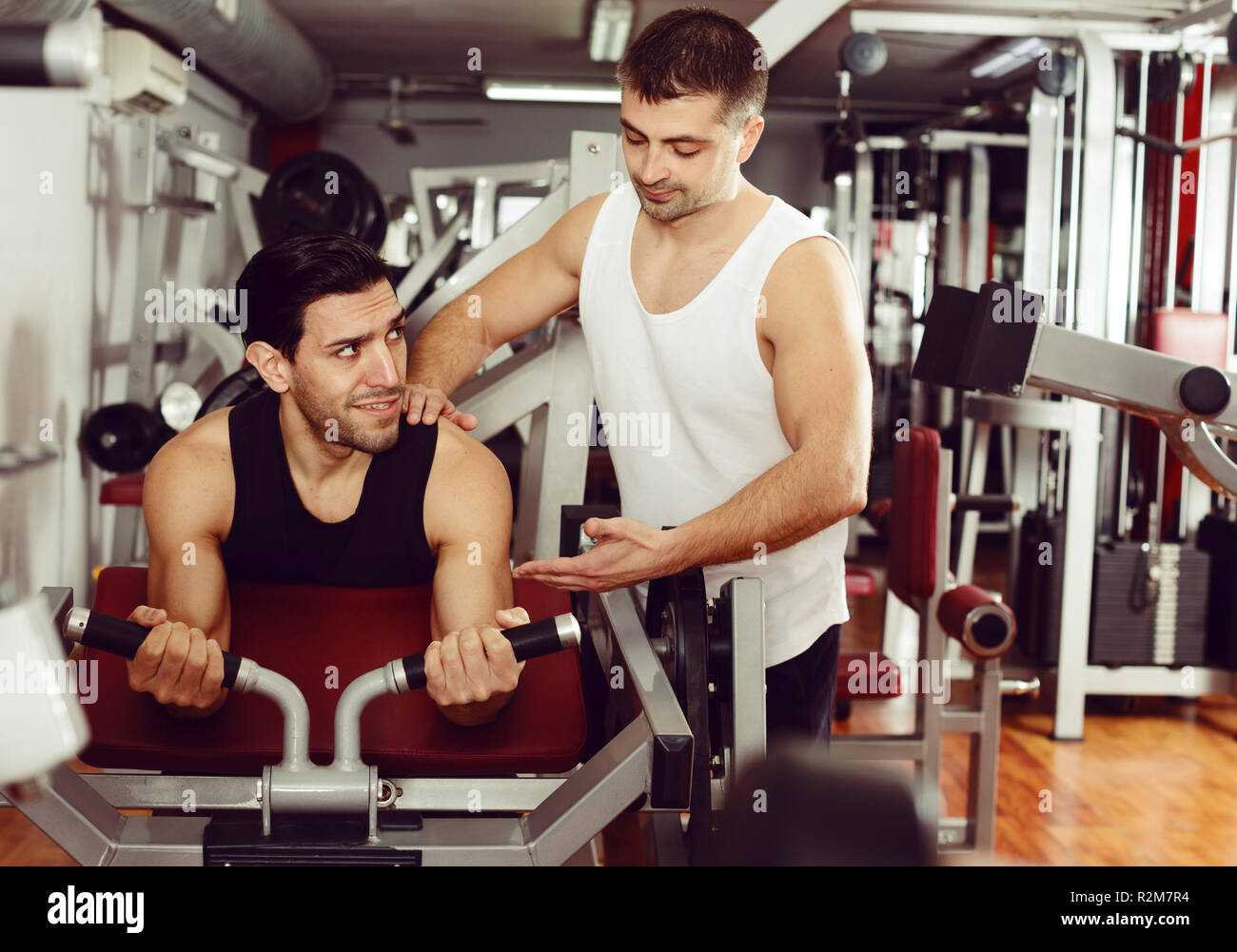 Male trainer explaining to muscular guy technique of performing ...