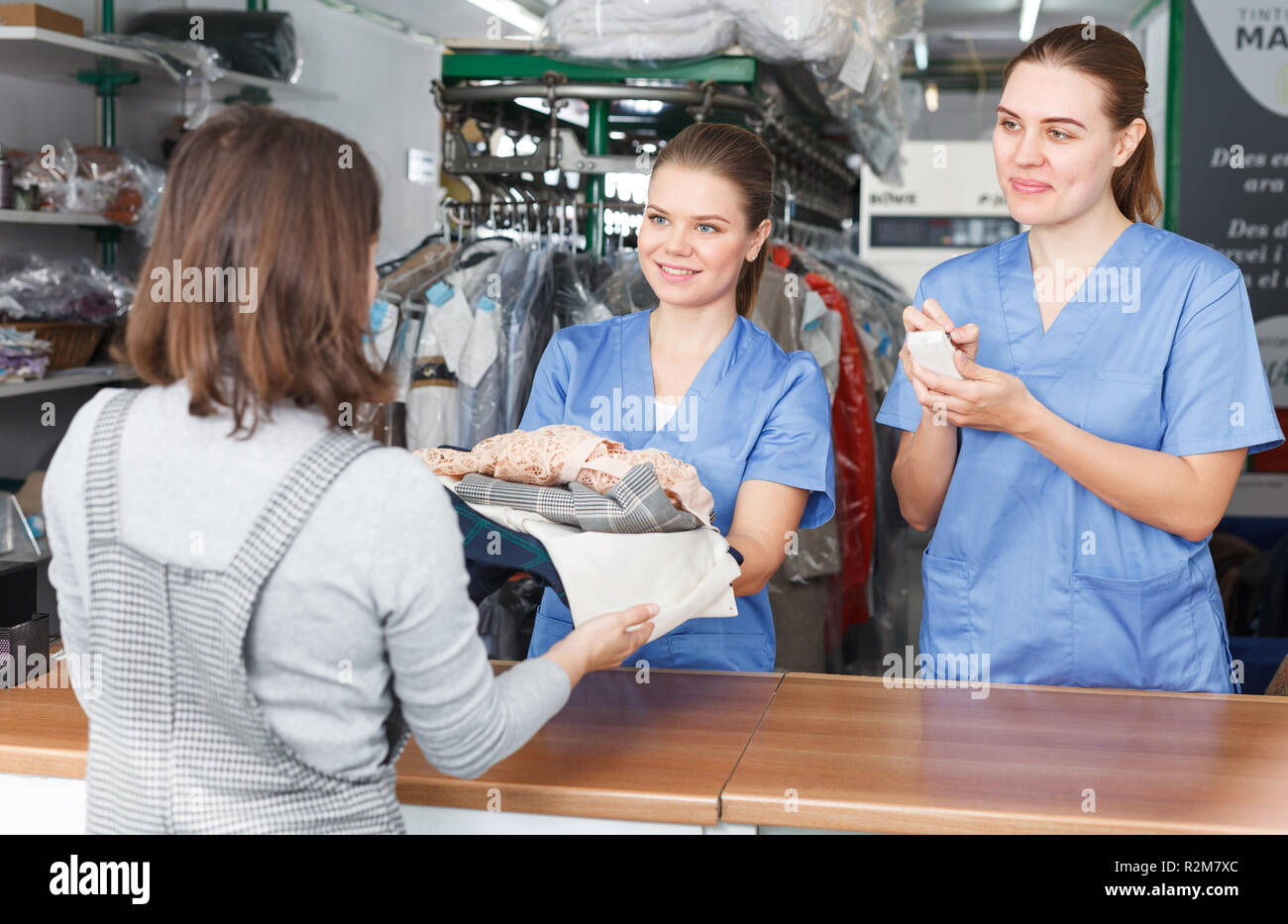 Female worker of dry cleaner checking clothes of customer on reception ...