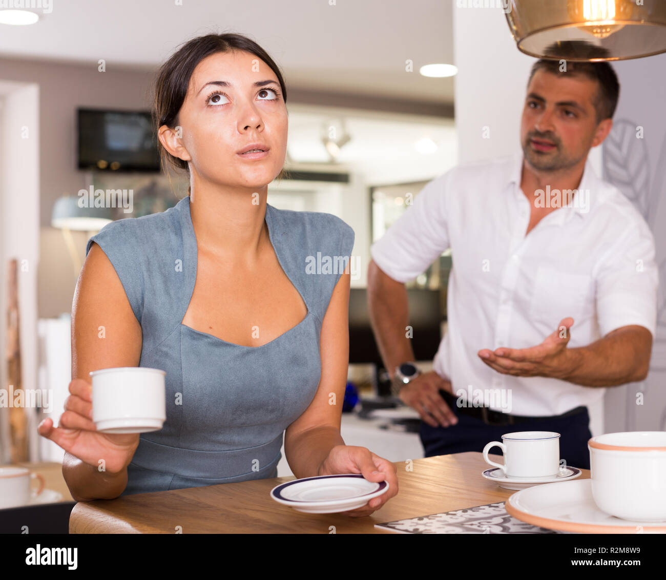 Frustrated girl sitting at home table with cup of coffee in hands on ...