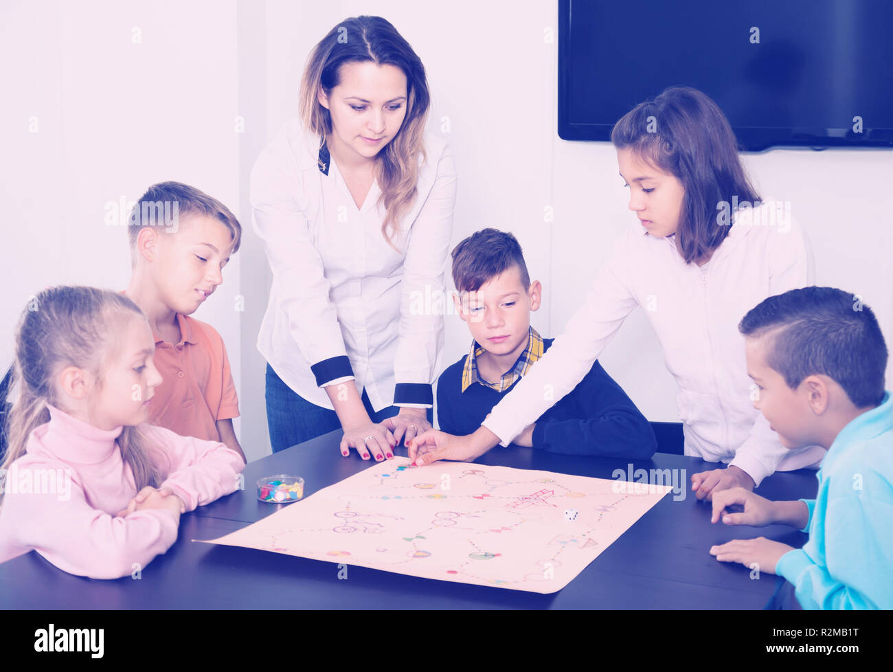 Smiling kids sitting at table with board game and dice at school Stock ...
