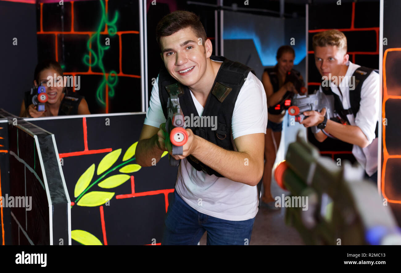 Group of young smiling people in vests and with laser pistols playing ...
