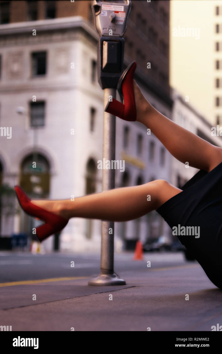 Legs of a woman who has fainted next to a parking meter on a busy city ...
