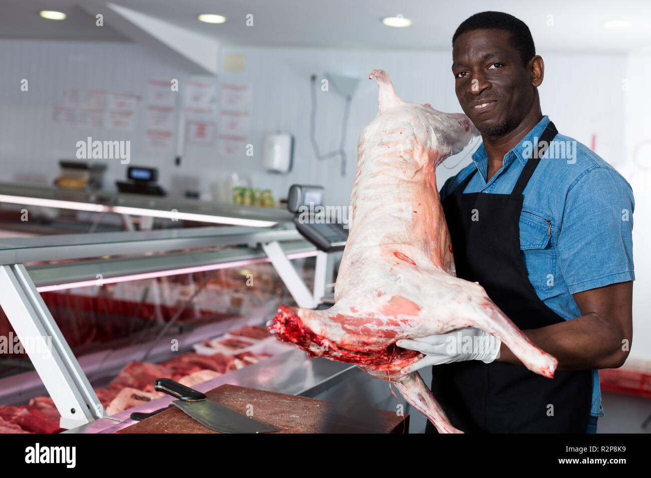 African American male butcher cutting lamb carcass in butcher shop ...