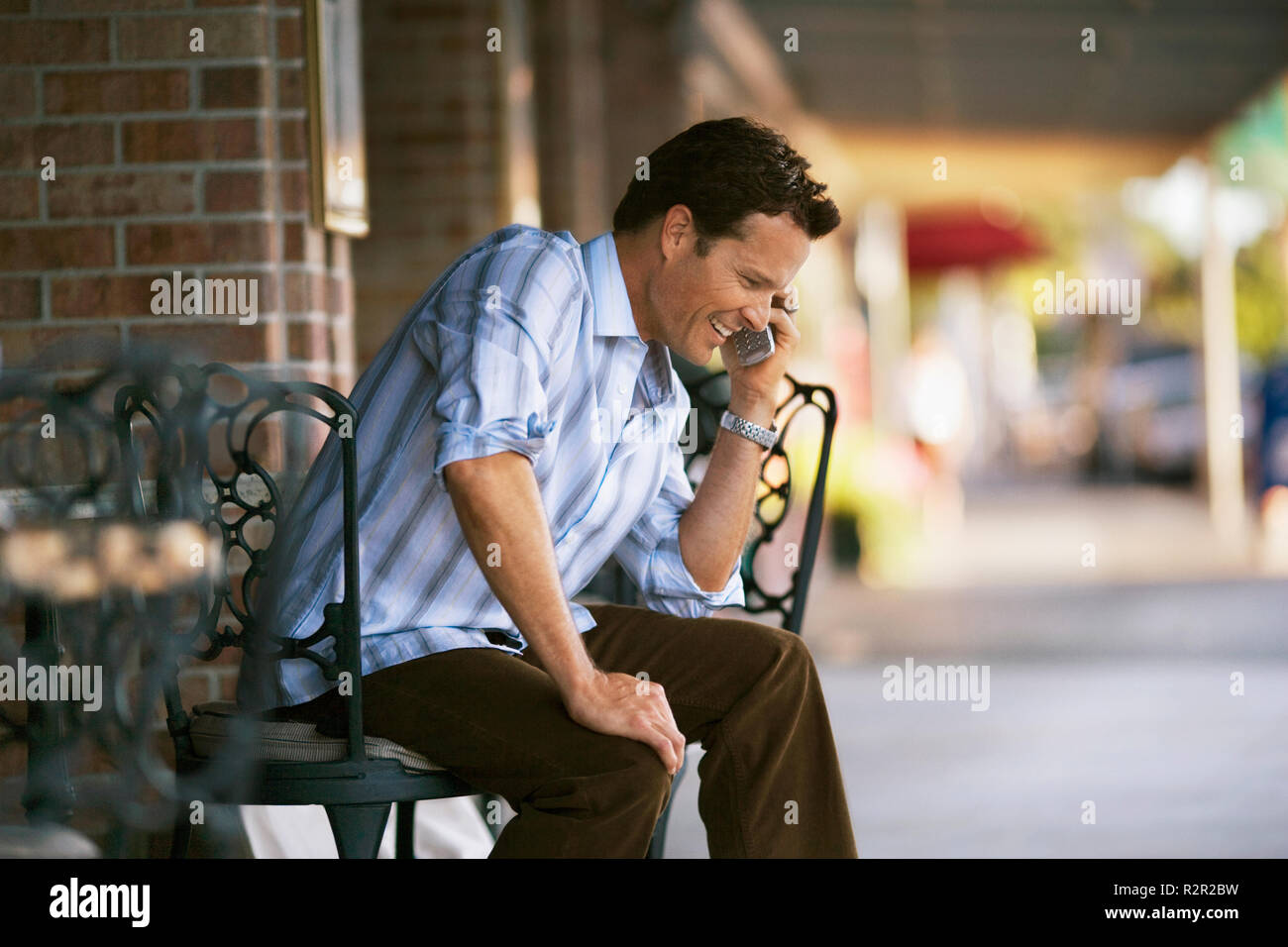 Mid-adult man sitting on a bench talking on a cellphone Stock Photo - Alamy