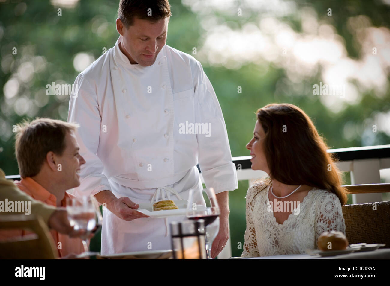 Happy mid-adult couple being served by waiters at an outdoor restaurant ...