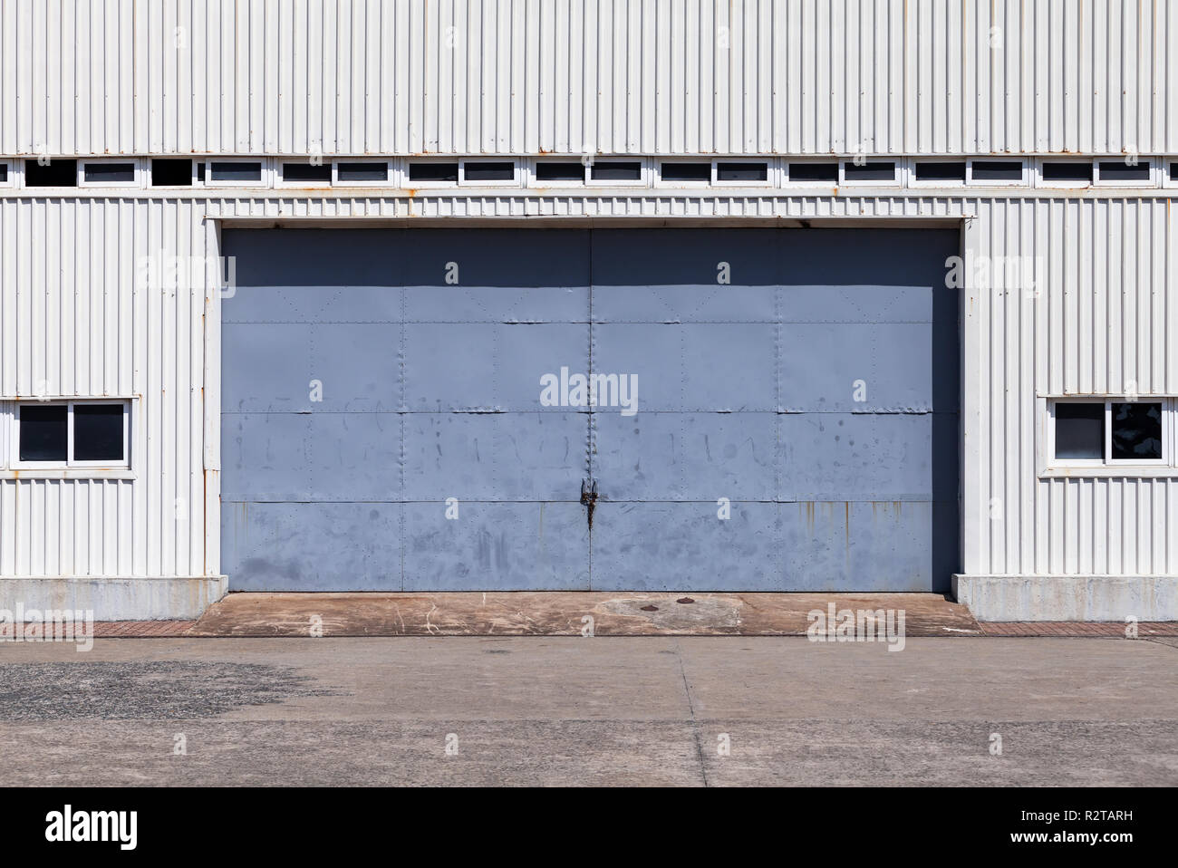 Closed blue gate in white ridged metal warehouse wall, flat background ...