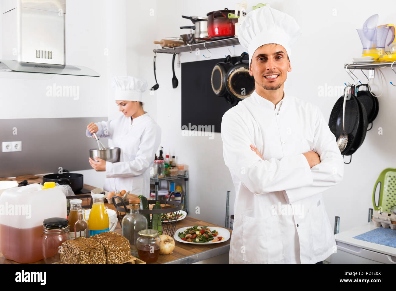 portrait of friendly smiling young male chef in white uniform at cafe's ...
