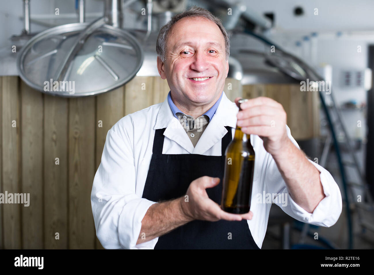 Brewer is standing with bottle for beer on his workplace indoor Stock ...