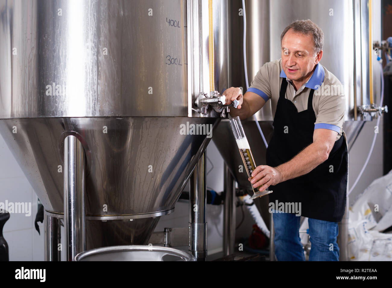 Happy cheerful smiling brewer is checking the quality of beer in flask ...