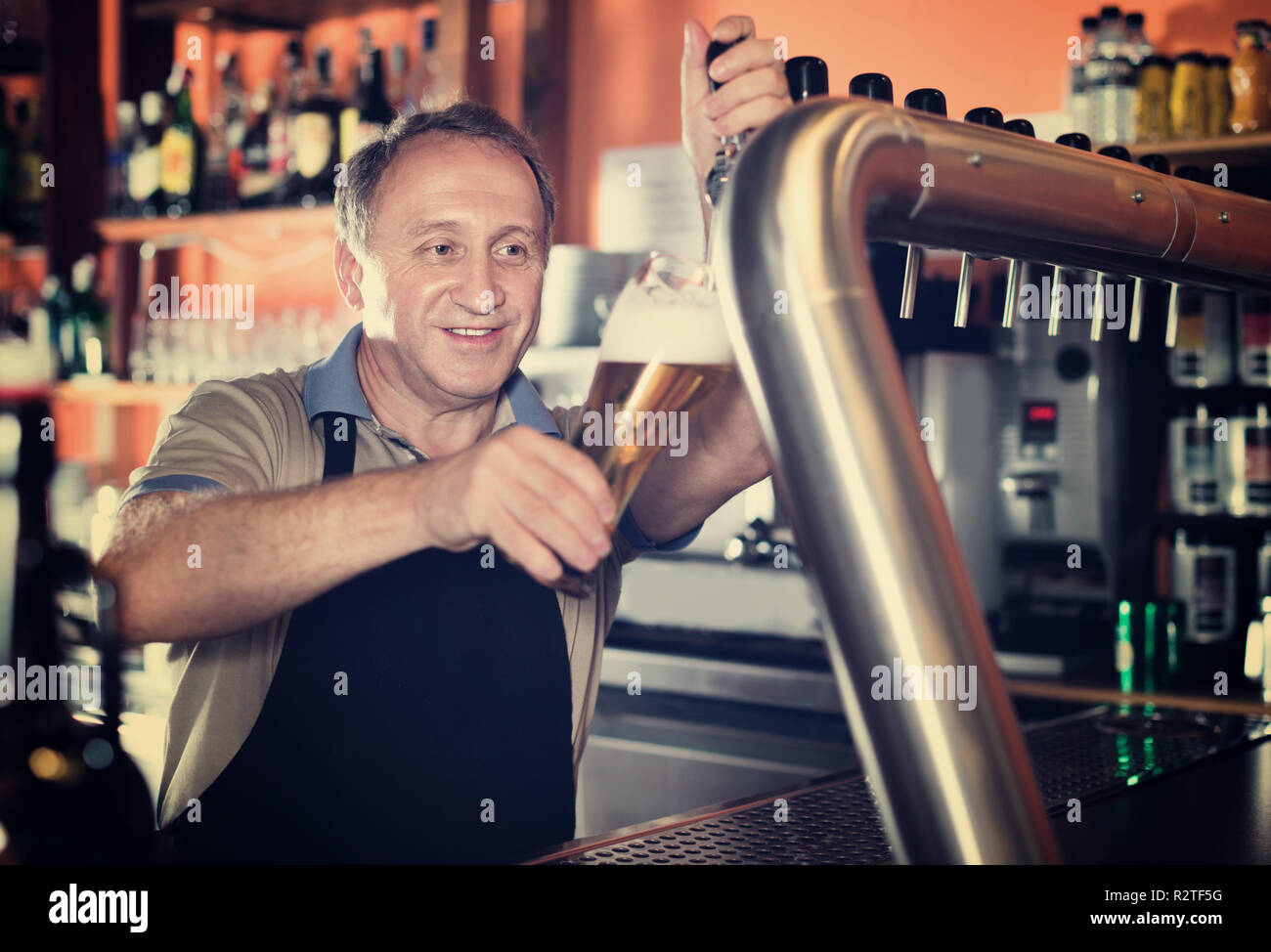 Smiling happy positive barman is pouring unbottled beer with foam for ...