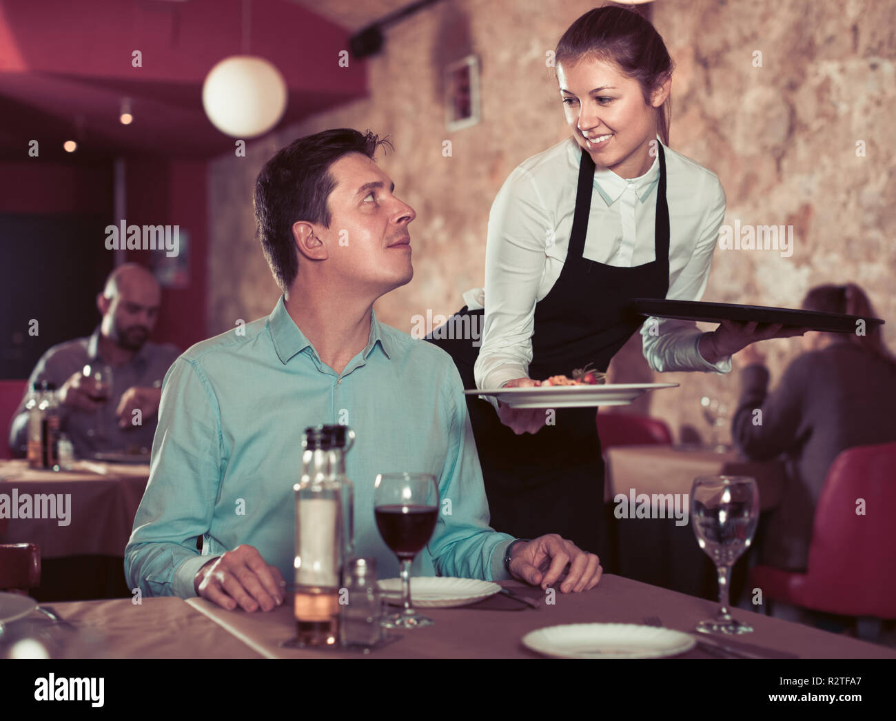 Positive waitress bringing delicious meal to young man in restaurant ...
