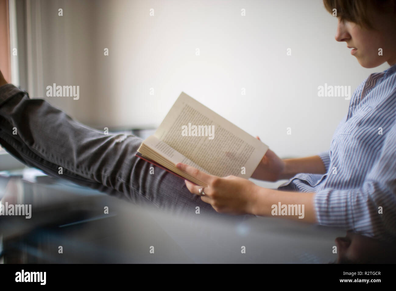 Young woman sitting reading a book with her legs stretched out Stock ...