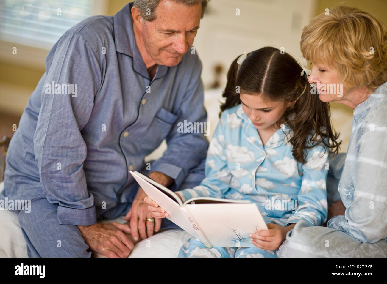 Grandparents with granddaughter in pyjamas reading book together Stock ...