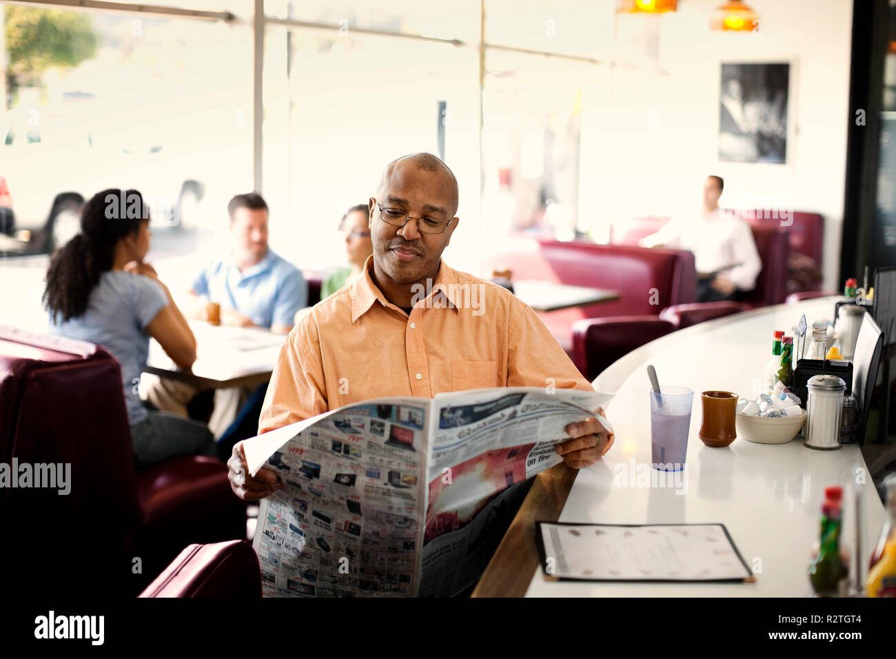 Happy mid adult man reading a newspaper in a diner Stock Photo - Alamy