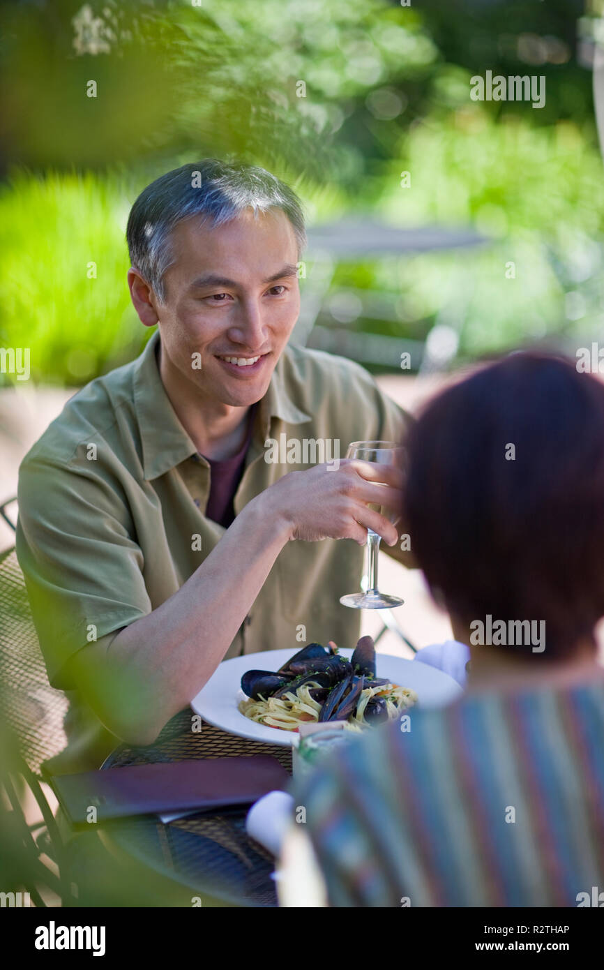 Smiling mid-adult man sitting at an outdoor table in a restaurant with ...