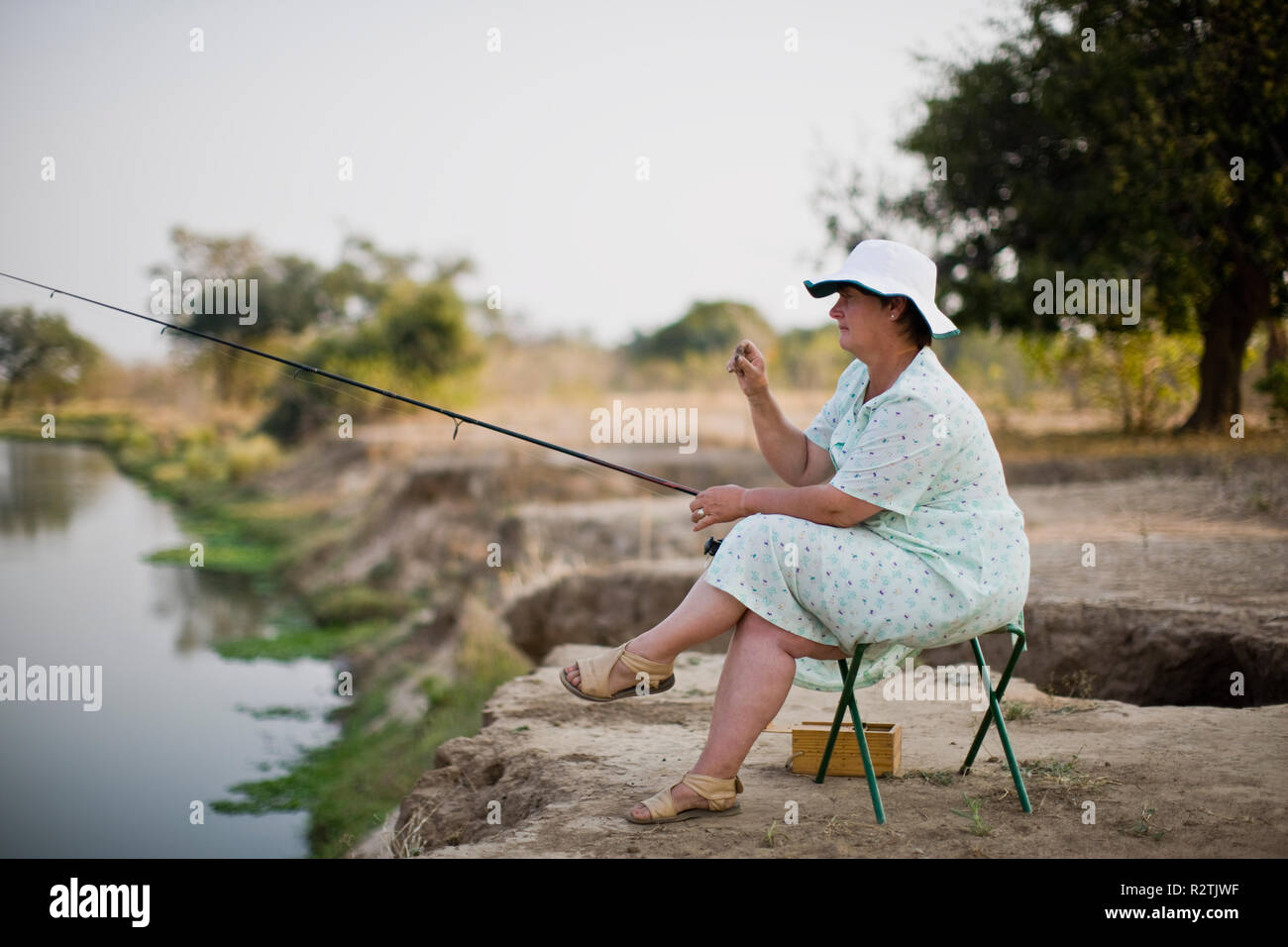 Mature woman sitting fishing by a lake Stock Photo - Alamy