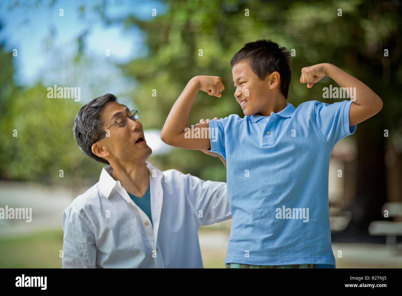 Playful young boy flexing his muscles while his proud father looks on ...