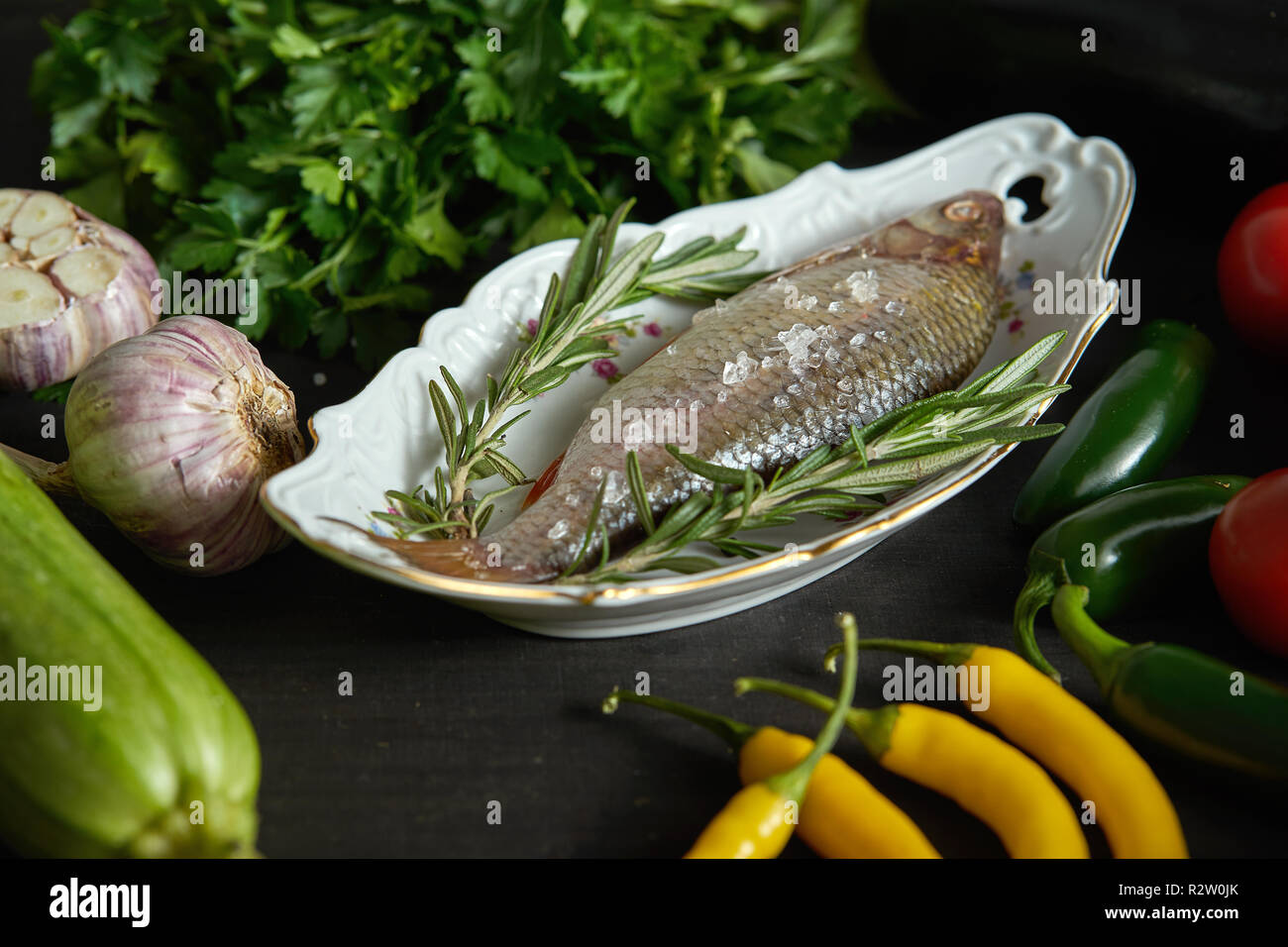 one fresh raw dorada fish in a white dish with a set of vegetables on a ...